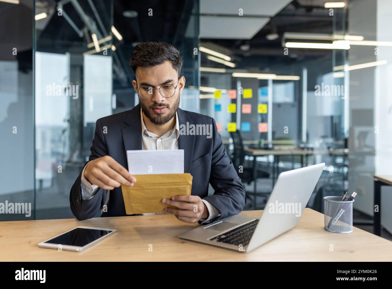 Serious man in office holding postal envelope, engaged in reading ...
