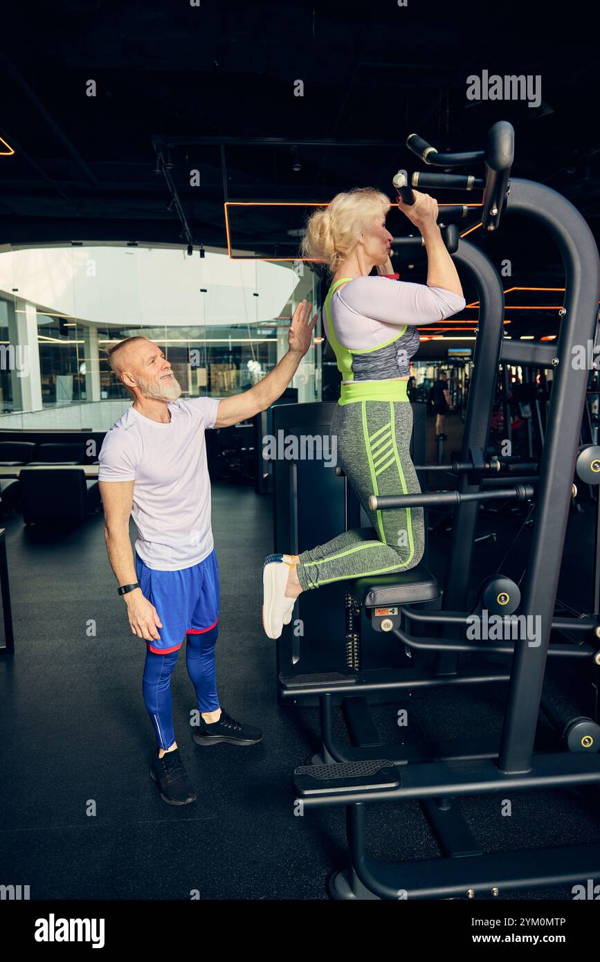 Senior woman practicing pull-ups with support from her partner in ...