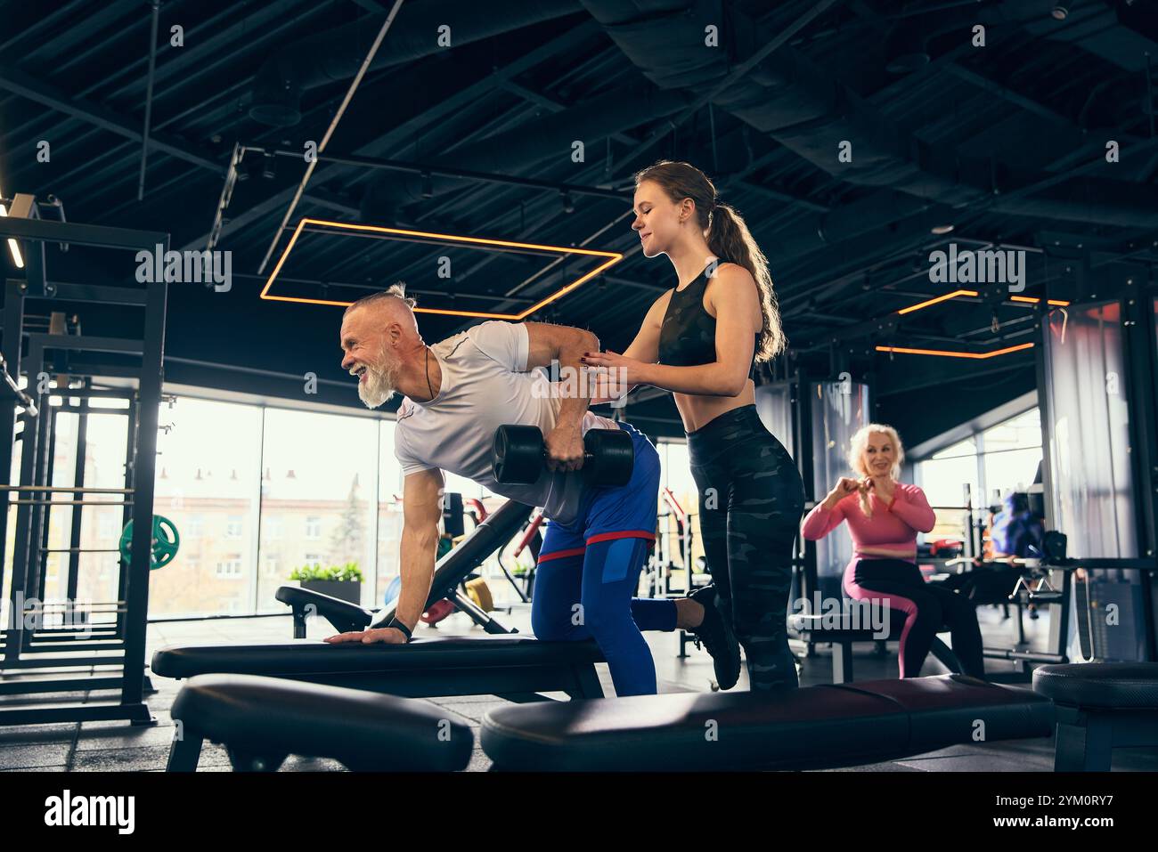Young woman, fitness trainer assisting senior man during dumbbell row ...