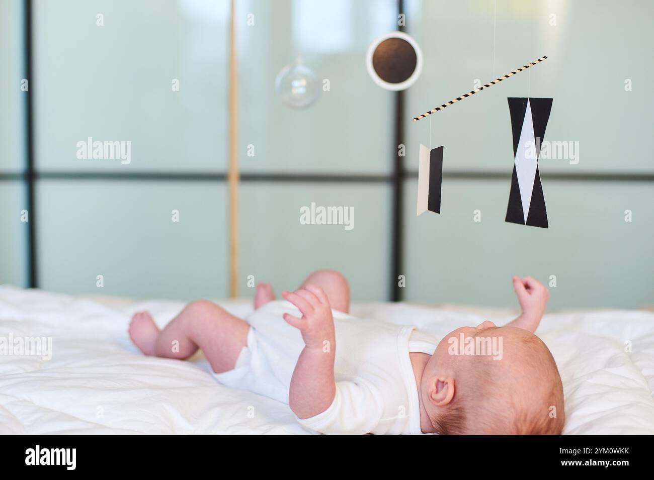 Newborn baby lying on a soft bed, reaching for a black and white ...