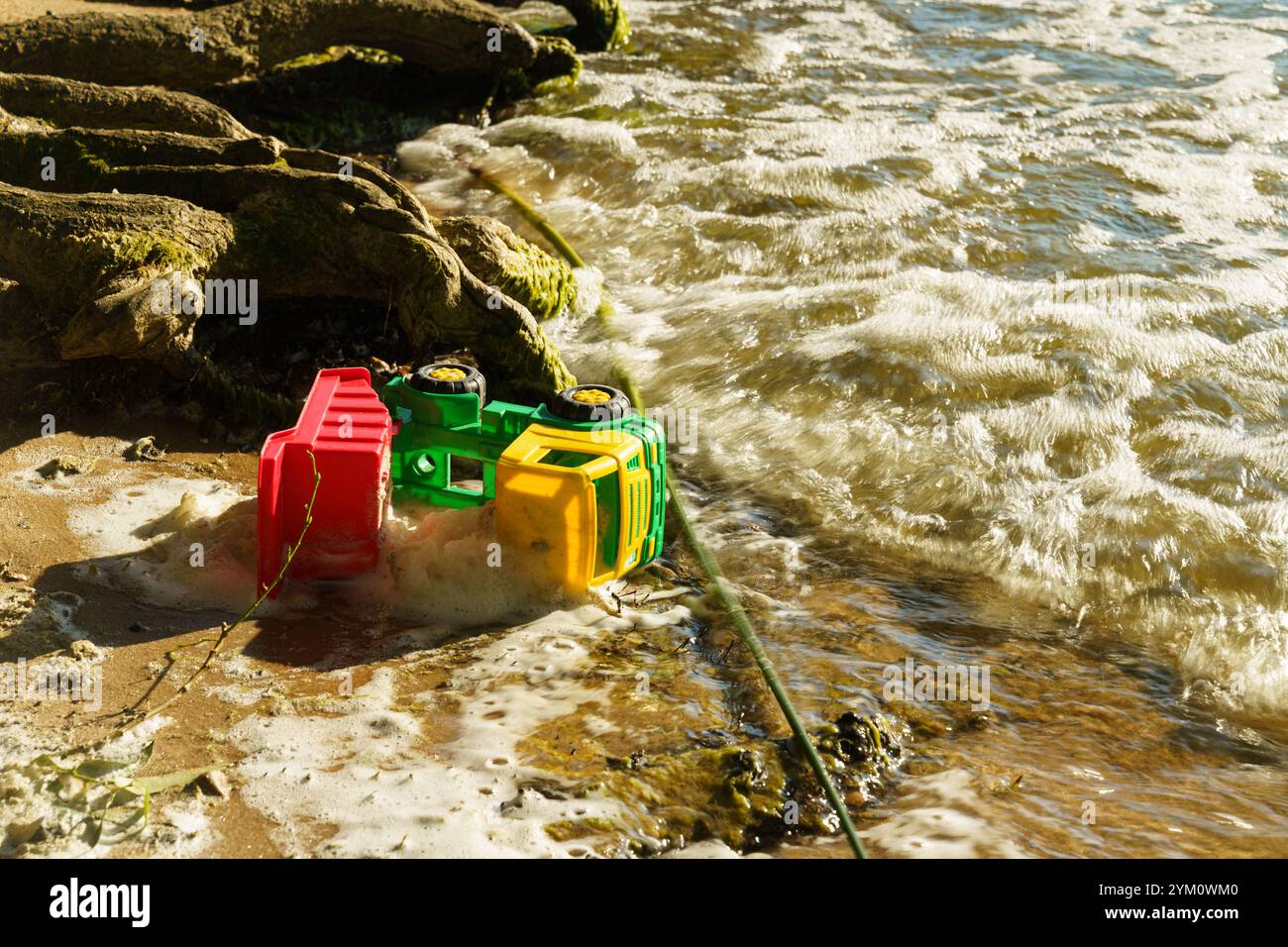 A vibrant toy truck rests on the sandy shore, partially submerged as ...