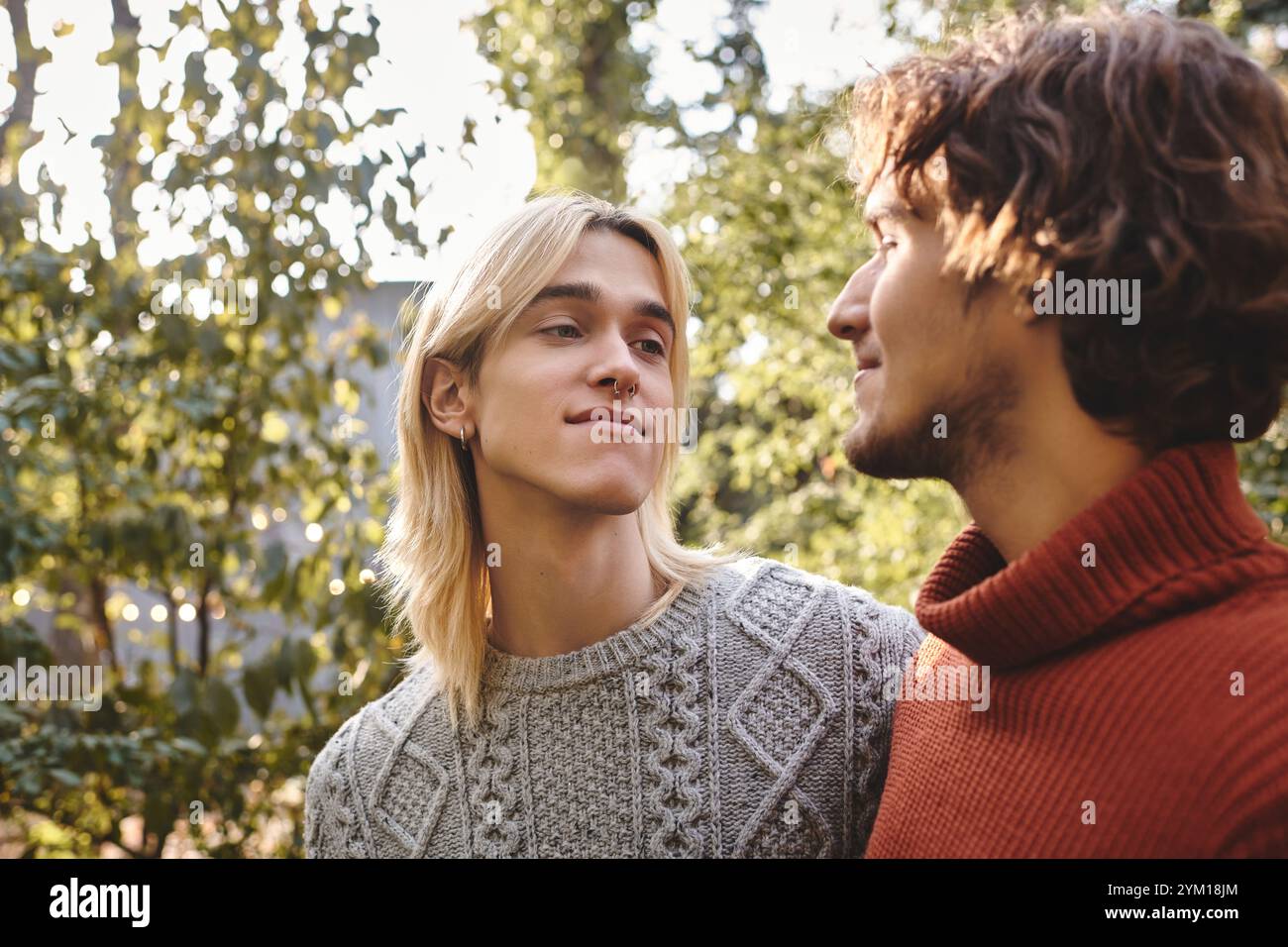 Two handsome young men share a heartfelt glance in a lush garden filled ...