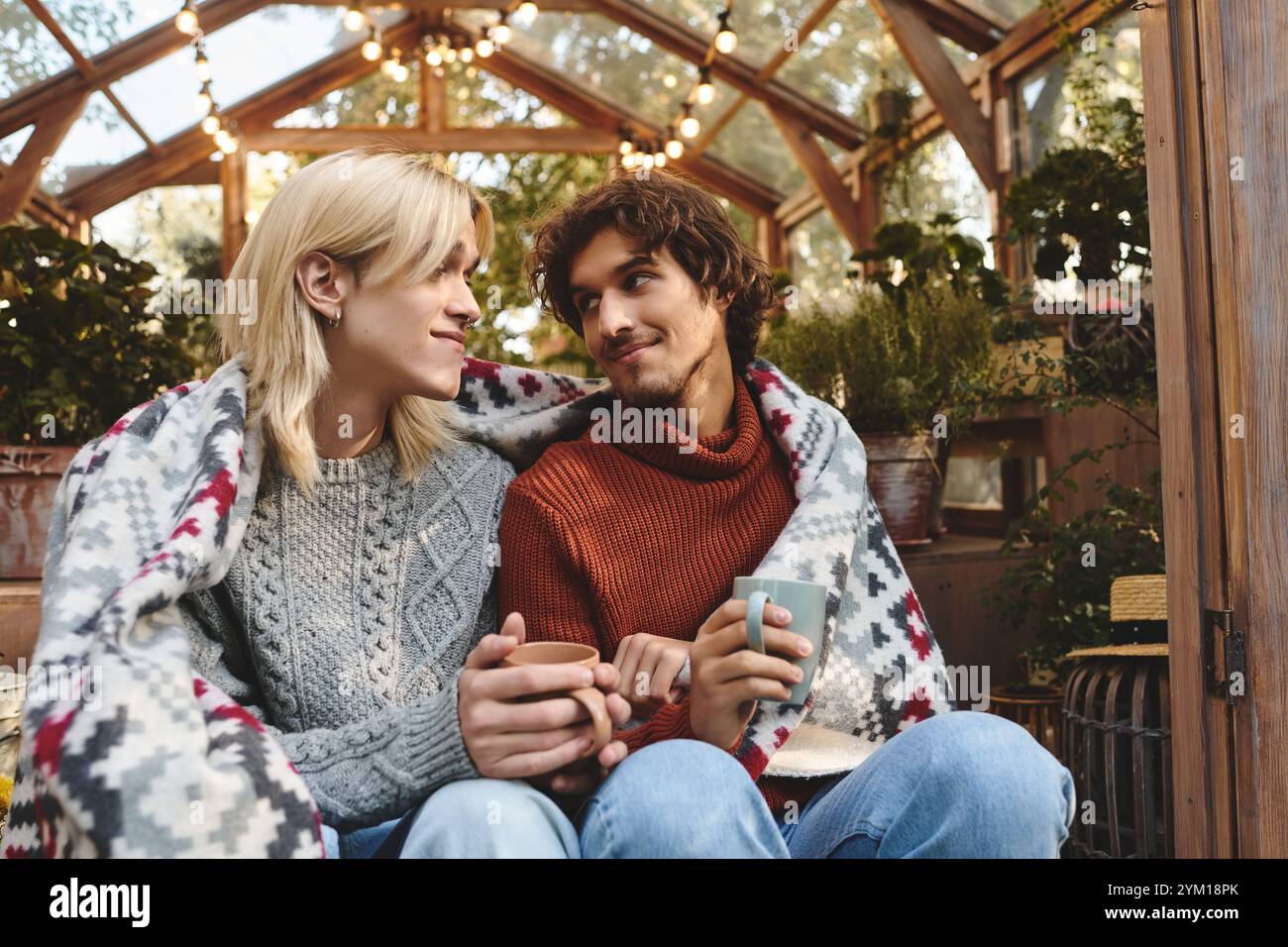 Two young and handsome people sit close together, wrapped in a cozy ...