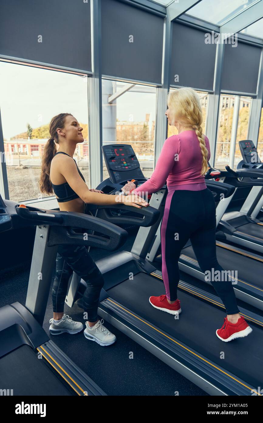 Young woman, fitness trainer monitoring senior woman as she walks on ...