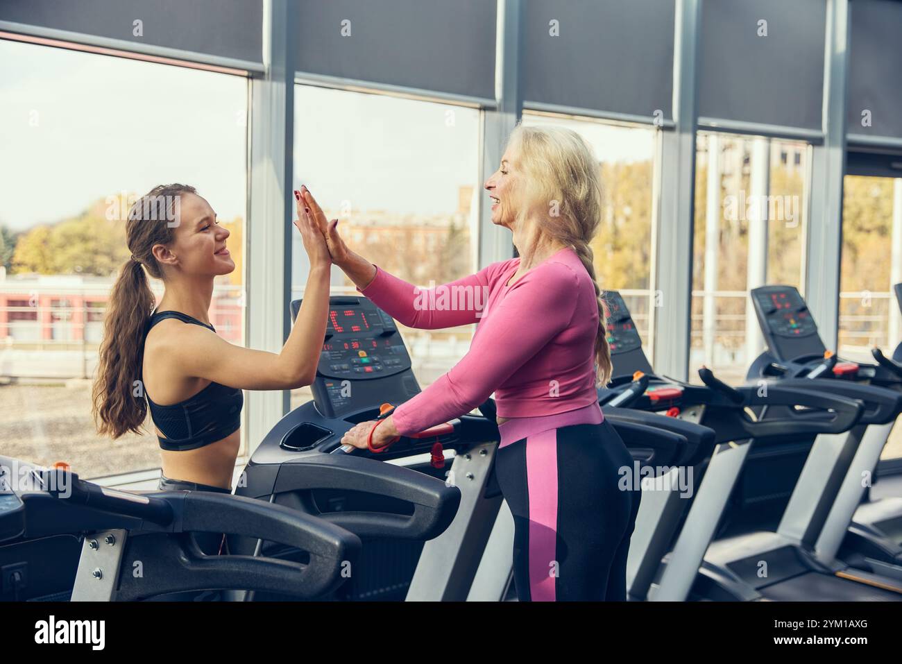 Senior woman and her fitness trainer sharing high five on treadmill ...