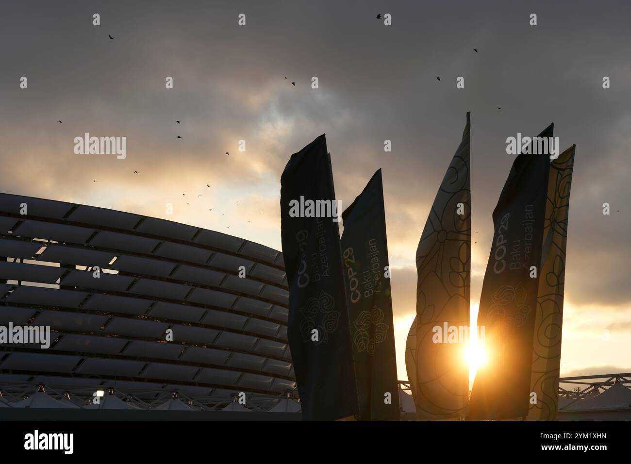 Birds fly over the Baku Olympic Stadium as the sun sets at the COP29 U ...