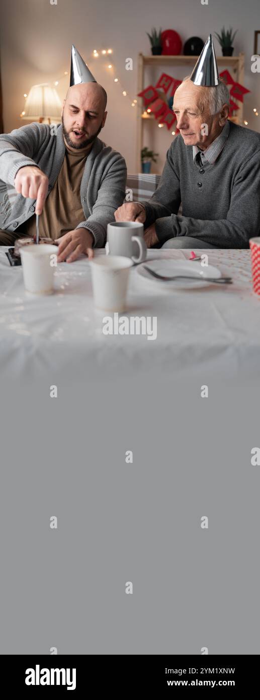 Son and old man father celebrating birthday at home young man cutting ...