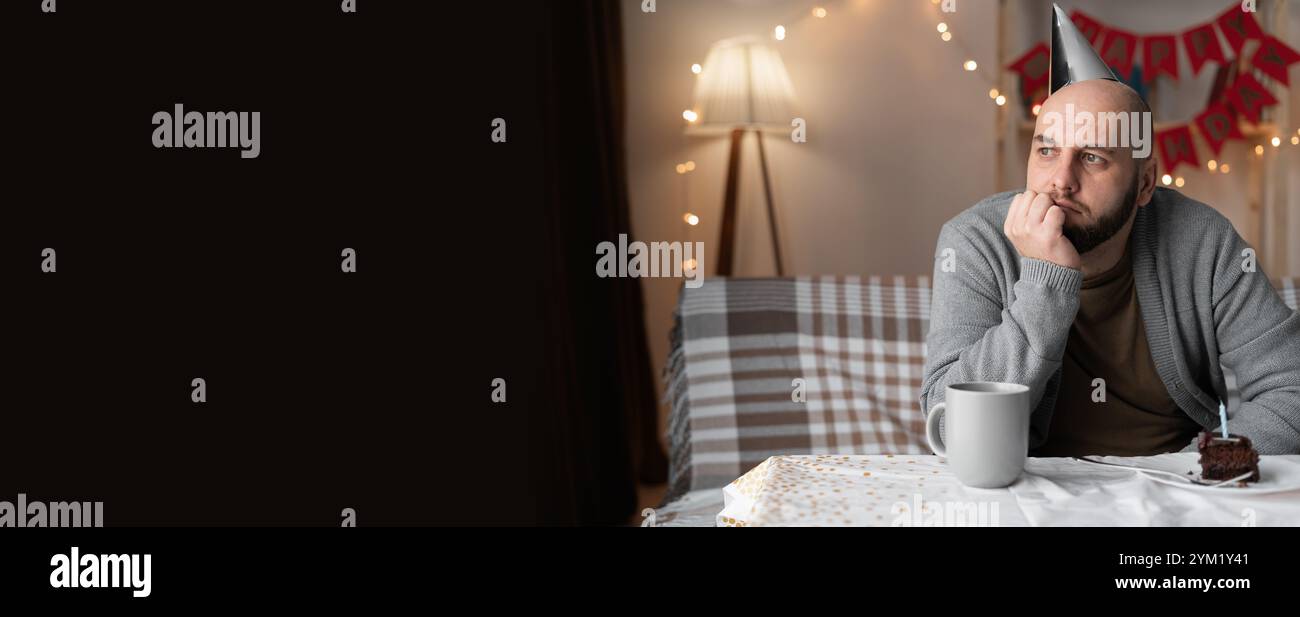 Sad man in party hat sitting alone celebrating lonely birthday at home ...