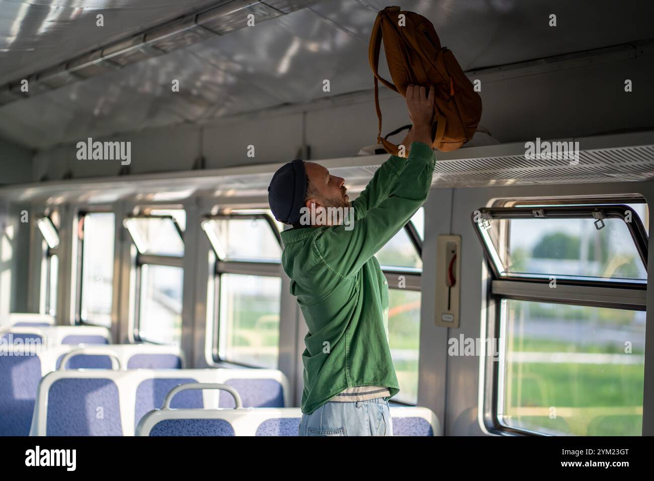 Man tourist lifts backpack onto overhead luggage rack in train. Solo ...