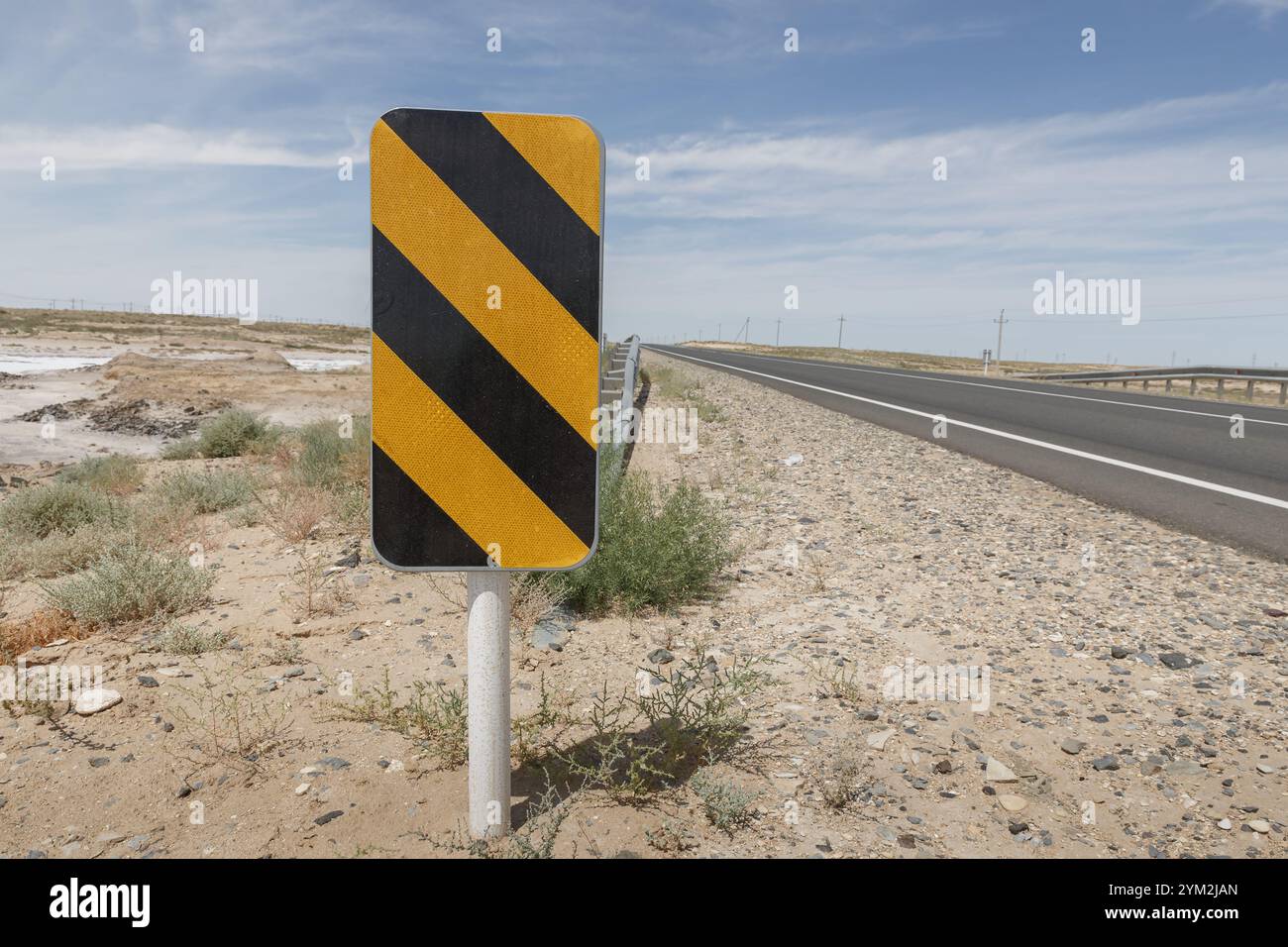 Road sign with yellow and black stripes on the roadside, warning sign ...