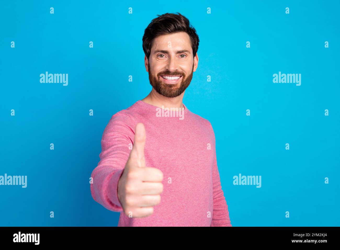 Confident man with a winning smile giving a thumbs up against a bright ...