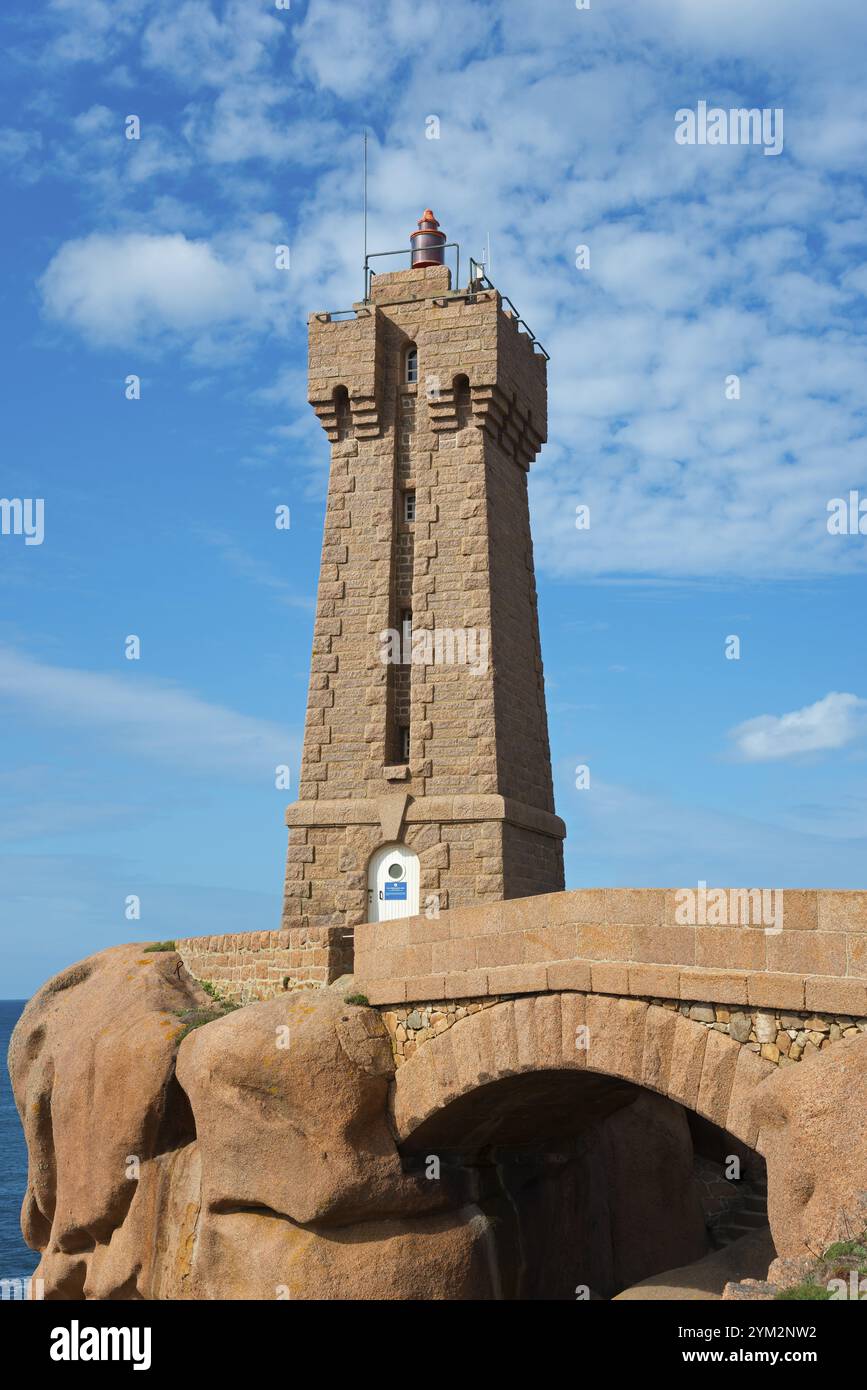 Lighthouse above an arch of rocks in front of a blue sky with clouds ...