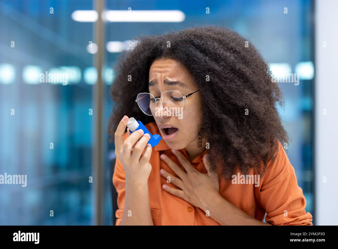 Concerned young woman using asthma inhaler in modern office. She holds ...