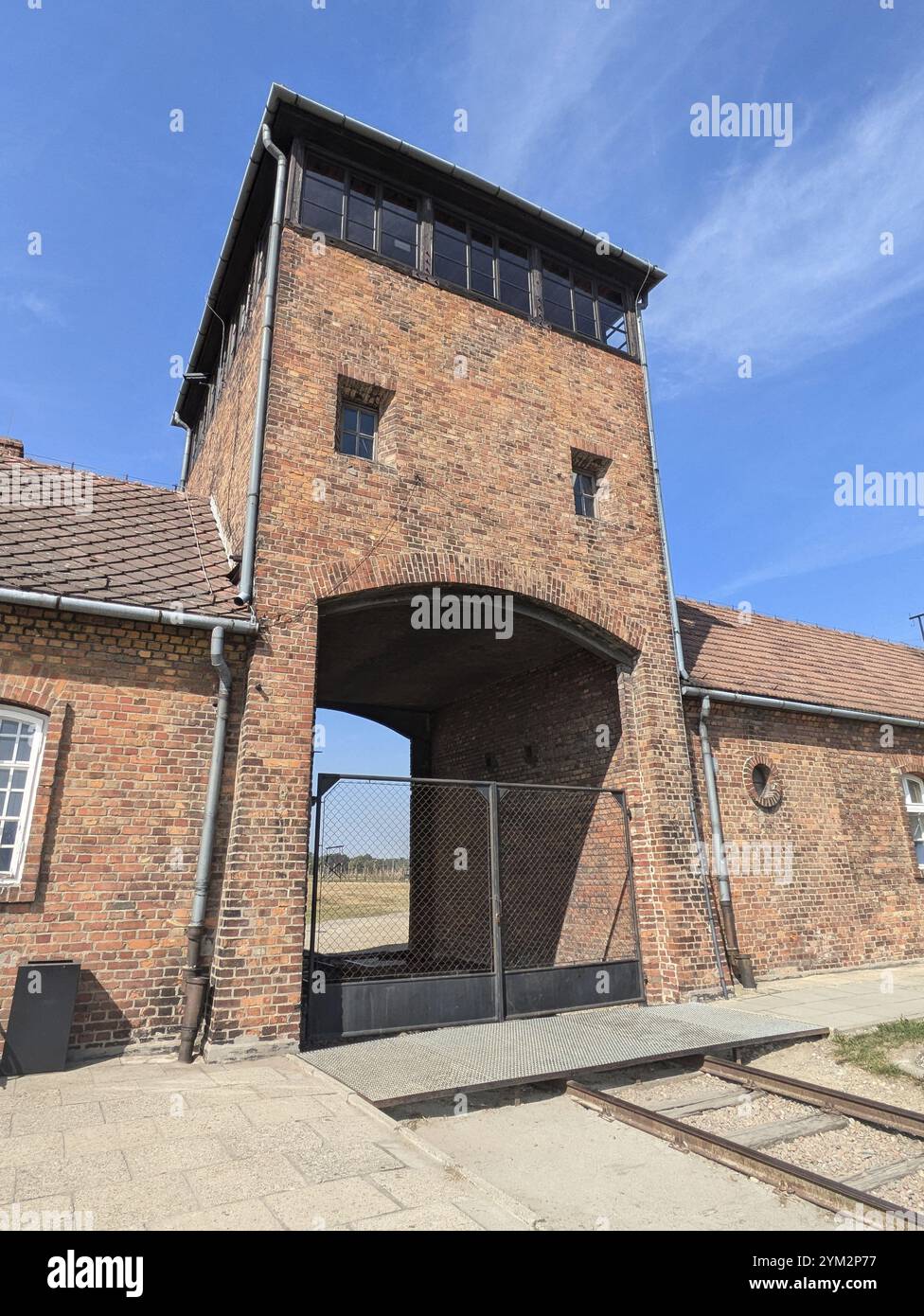 Historic brick entrance with a watchtower under a clear sky. Auschwitz ...