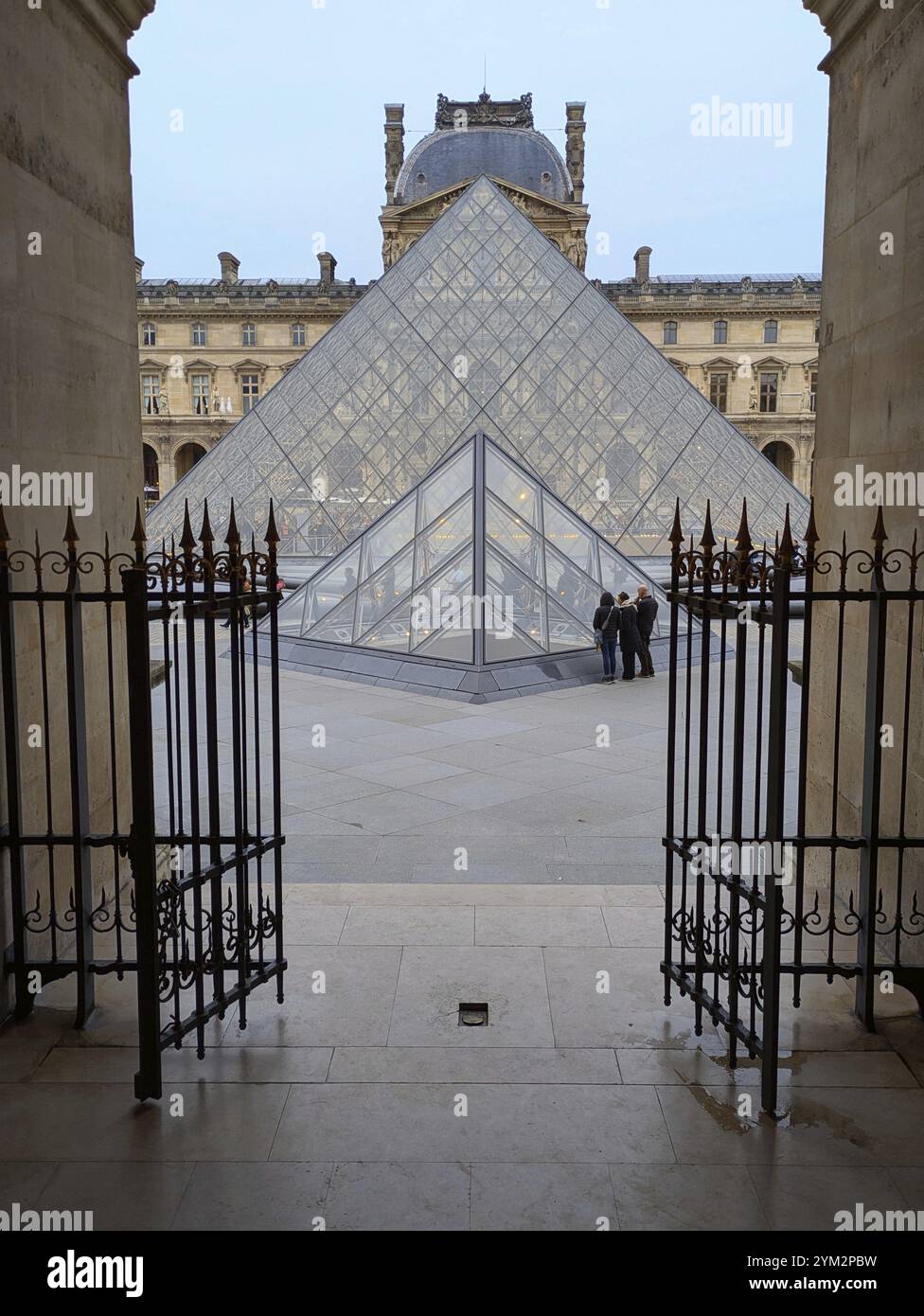 The glass pyramid of the Louvre visible through iron gates. Paris ...