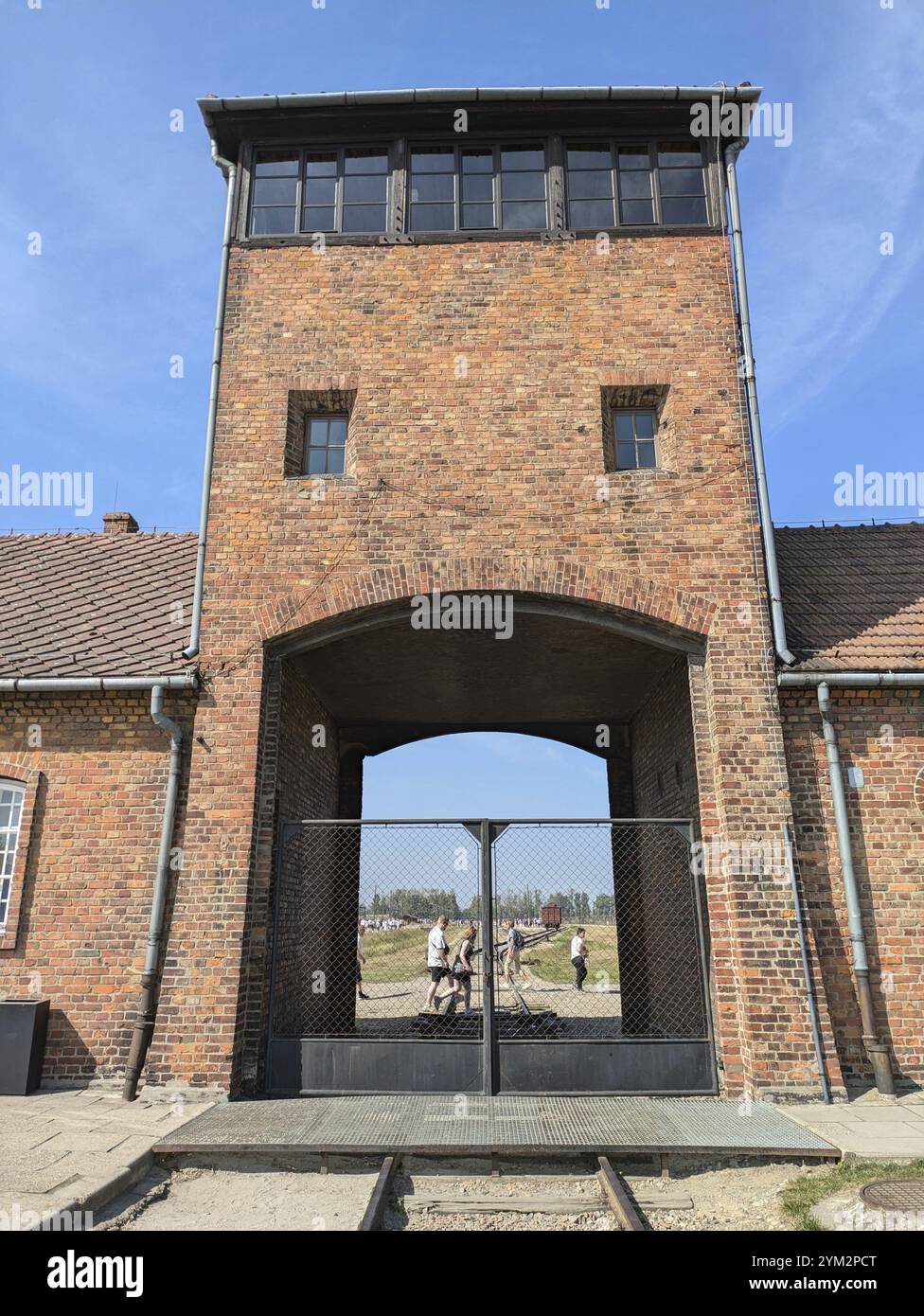 Brick watchtower with a metal gate under a clear blue sky. Auschwitz ...
