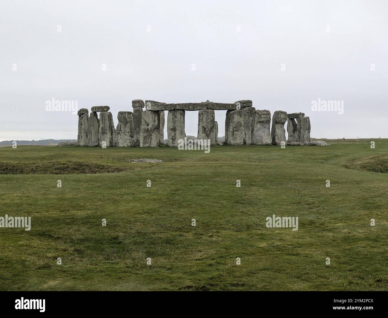 Distant view of Stonehenge with green grass under an overcast sky ...