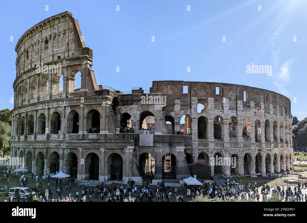 Side view of the Colosseum with tourists visible and sunlight ...