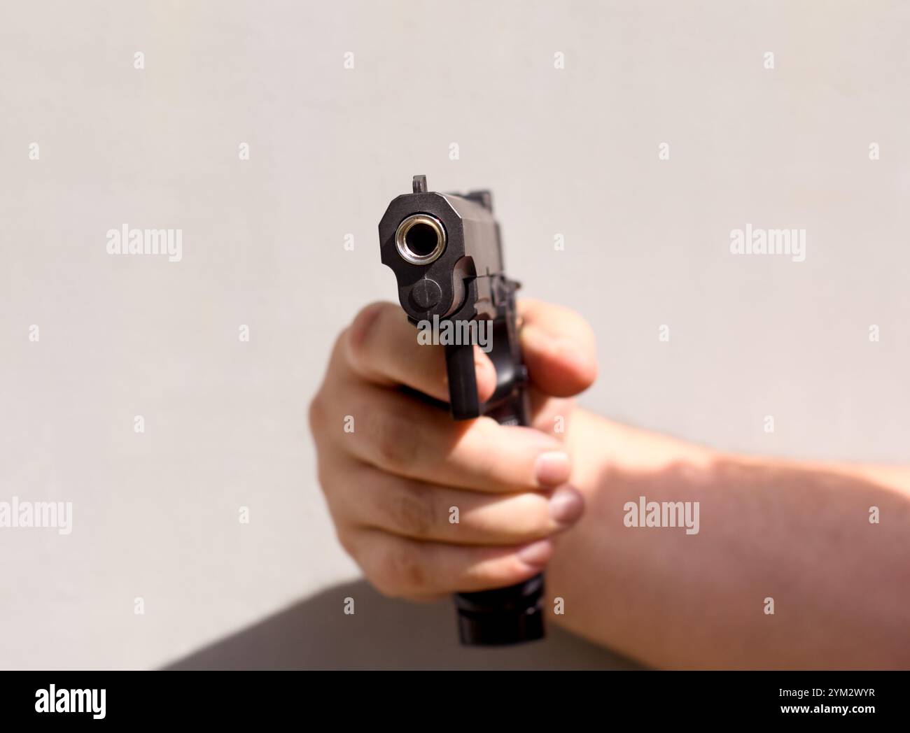 Hand holding a gun and pointing it at the camera on a light gray ...