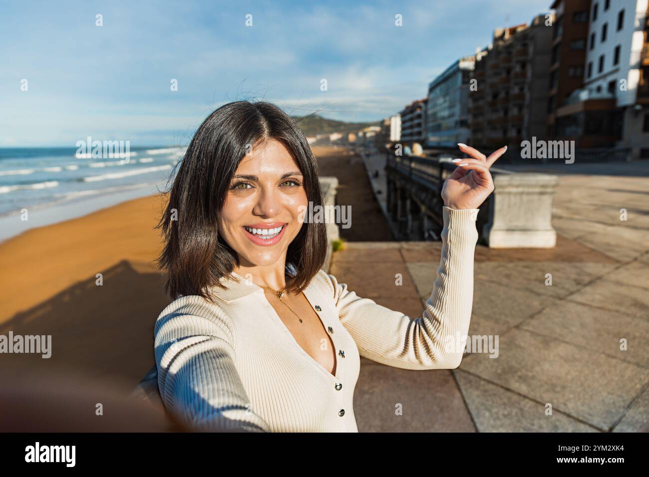 Smiling woman takes a selfie while pointing towards the beach ...