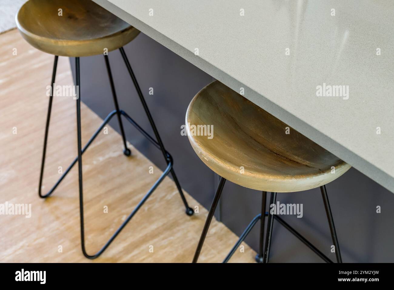 Two wooden stools sit on a countertop. The stools are black and brown ...