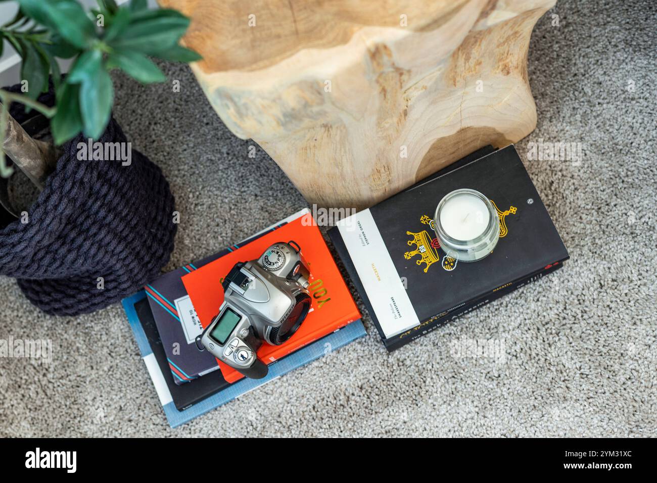 A camera sits on top of a stack of books and a candle. The camera is ...