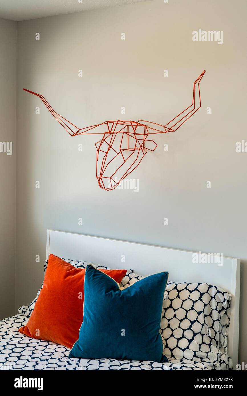 A red bull head is mounted on a wall above a bed. The head is made of ...