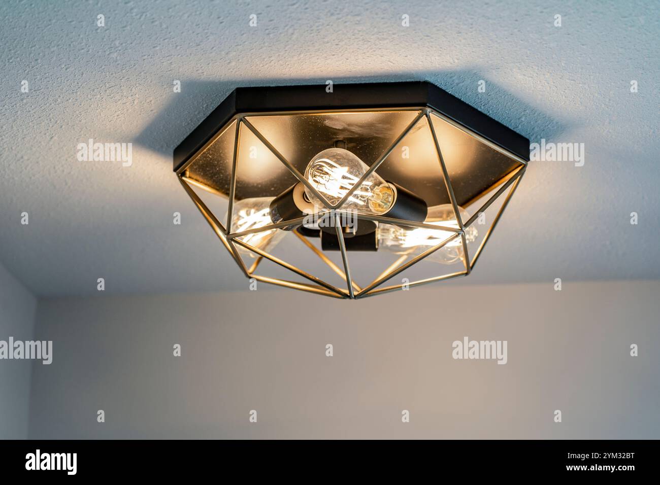 A light fixture with three bulbs is lit up. The fixture is made of ...