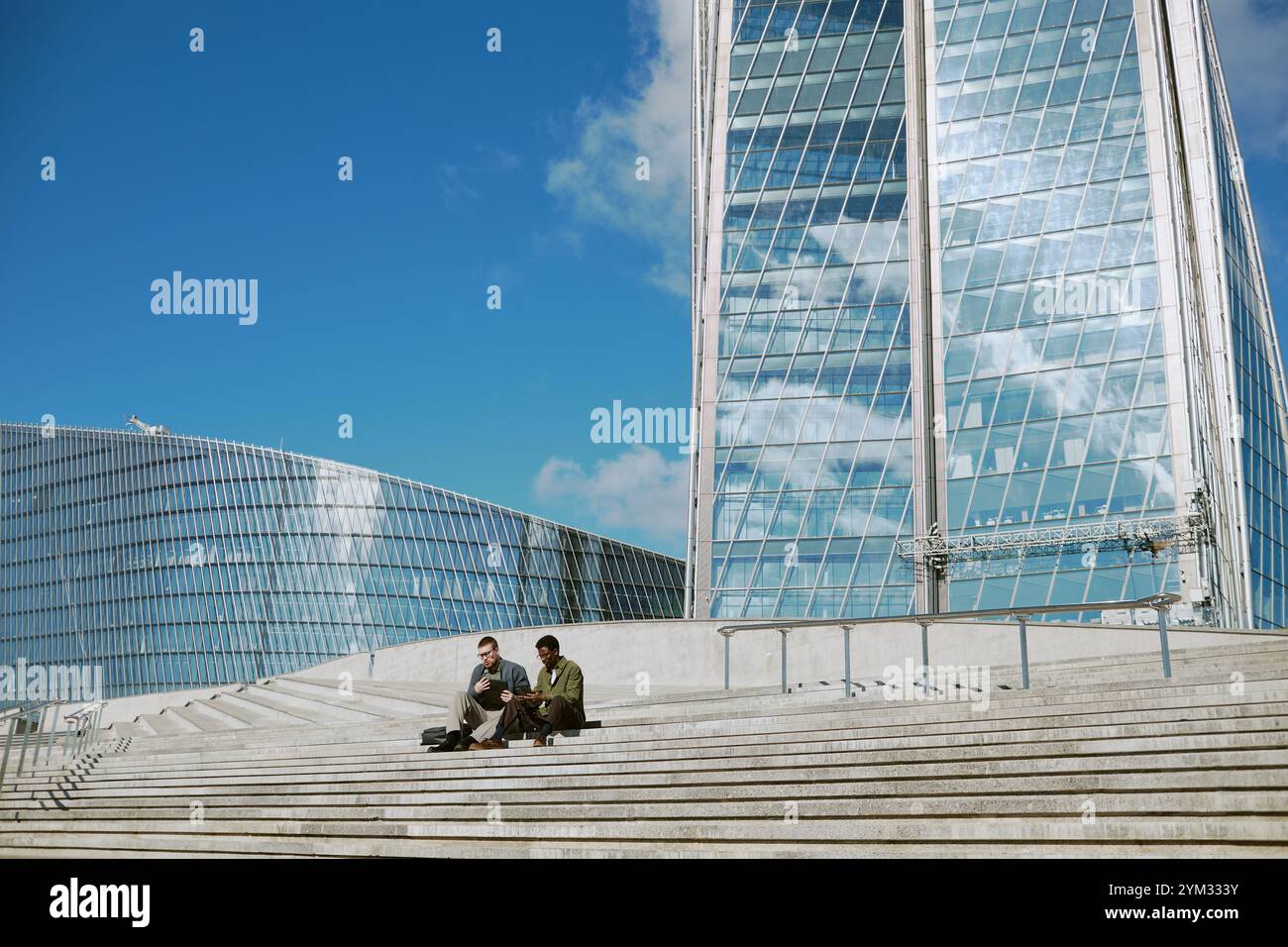 Two people sitting on stairs of a modern building with glass facades ...