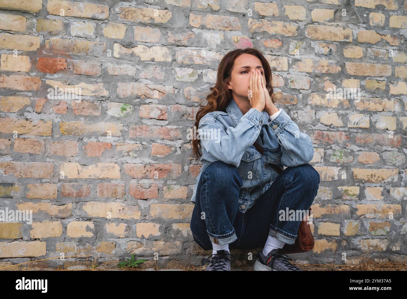 Alone stressed urban woman sits next to the brick wall on the street in ...