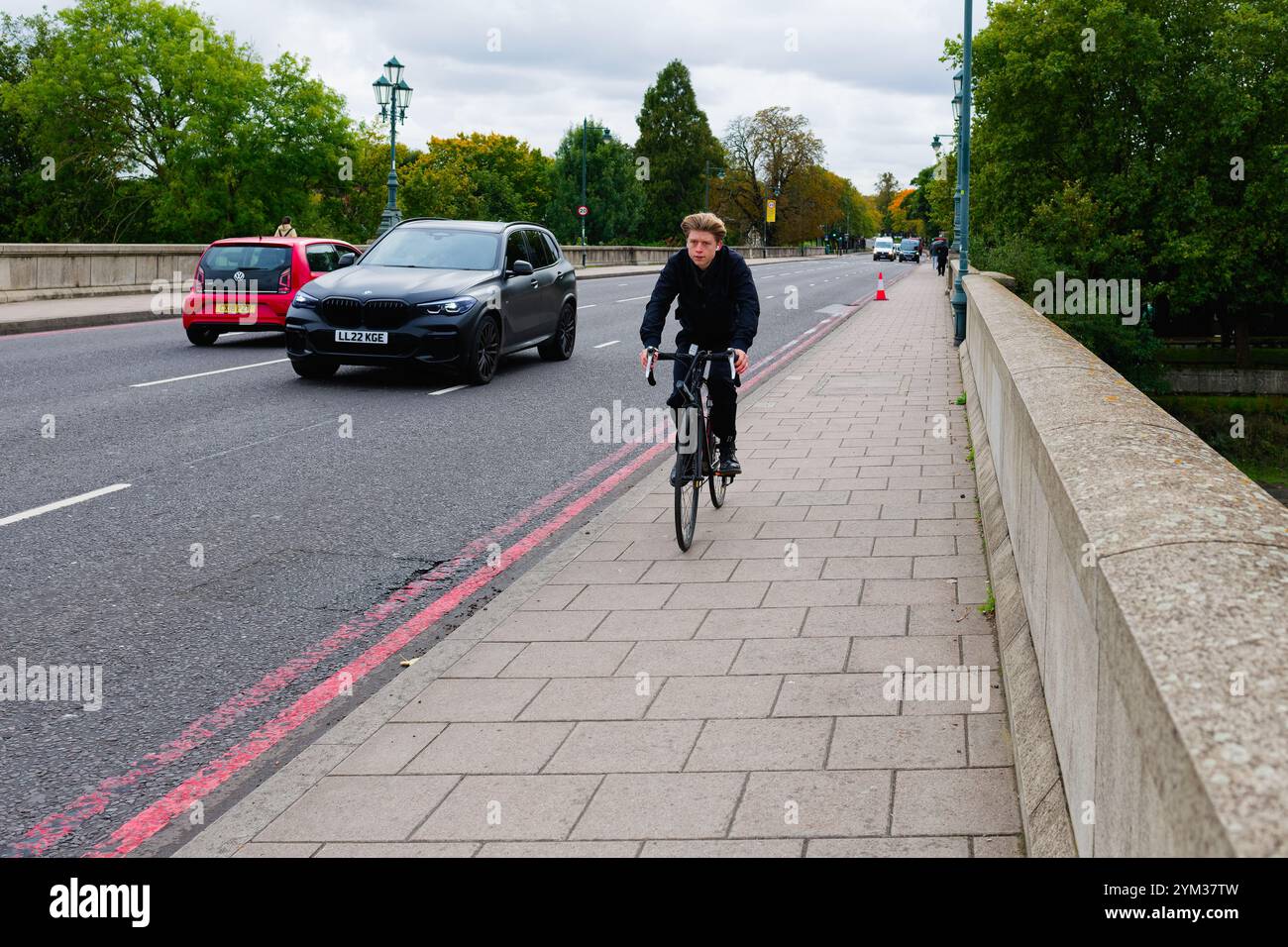 A young male cyclist riding his bike on the pavement on Kew Bridge West ...