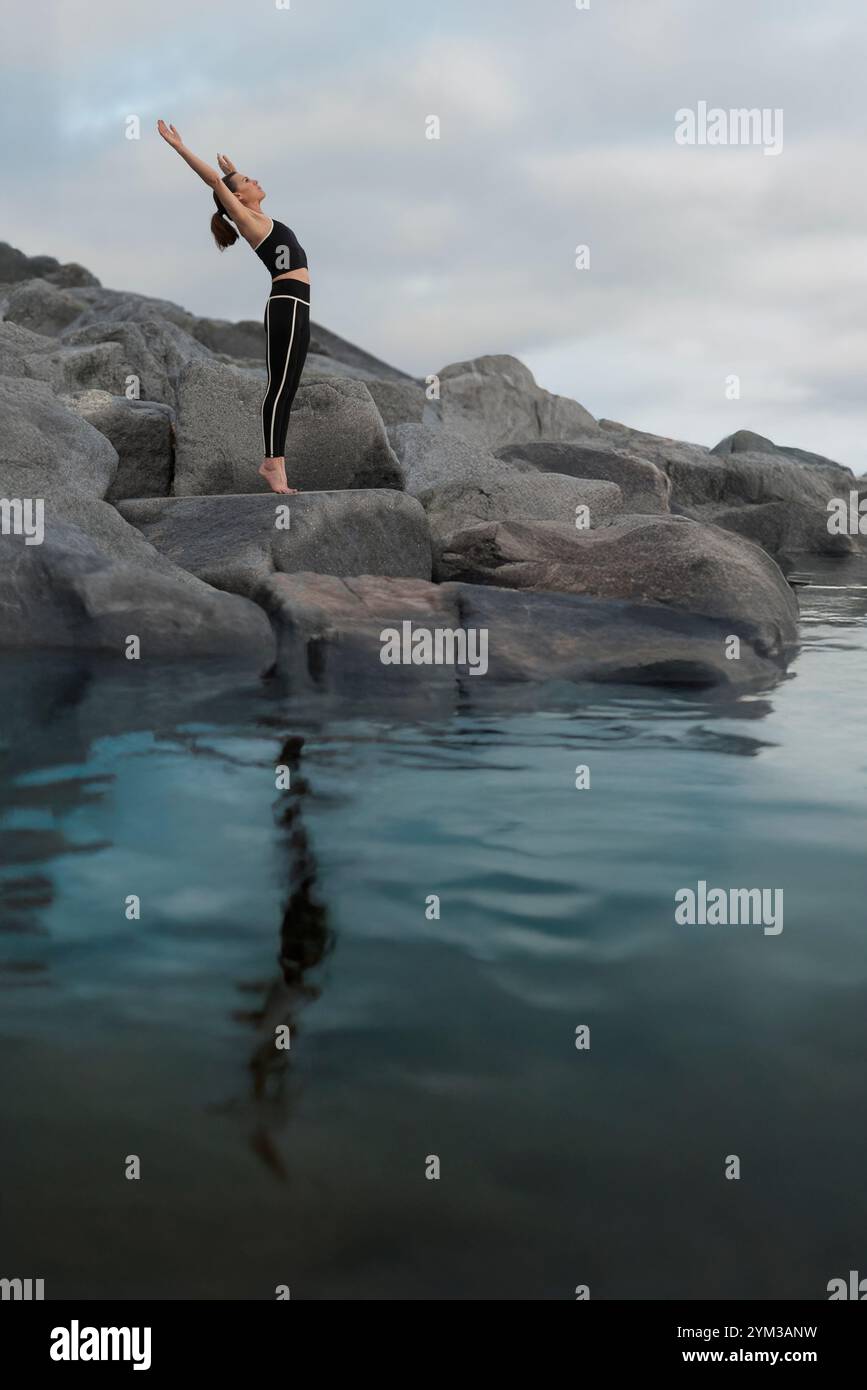 fit sporty woman standing on rocks by the sea doing stretching ...