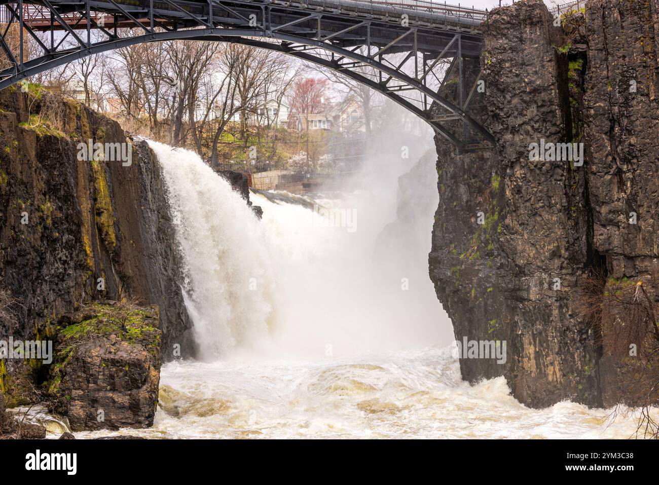 Powerful waterfall cascading between rocky cliffs with an iron bridge ...