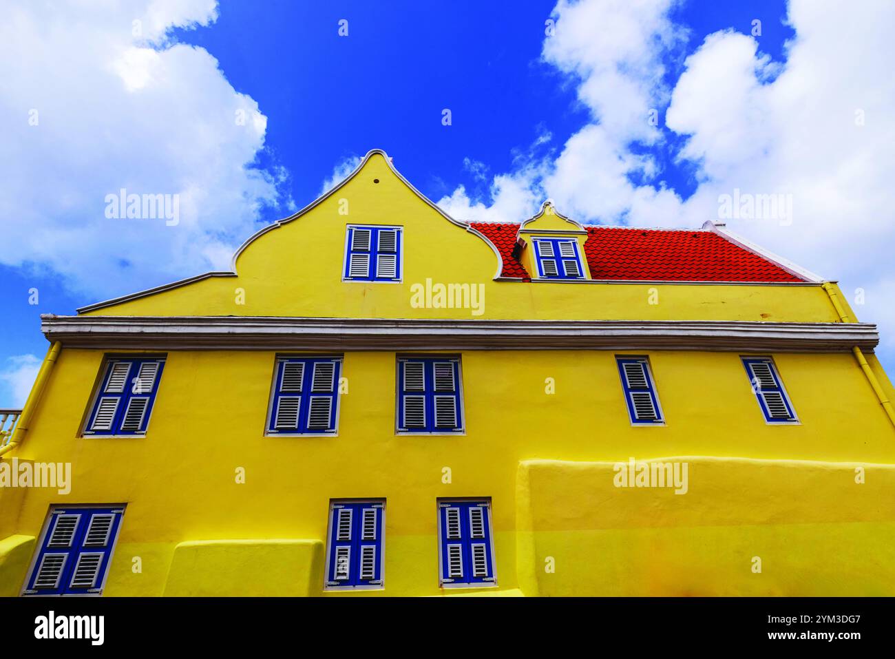 Bright yellow colonial-style building with red roof and blue shutters ...