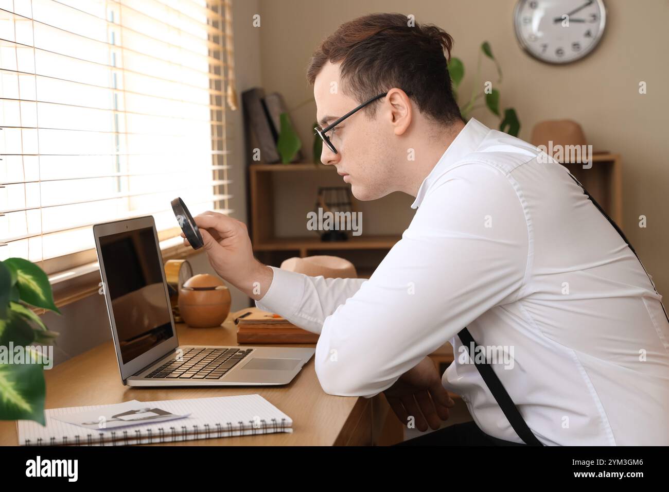 Male detective with magnifier examining laptop at table in office Stock ...