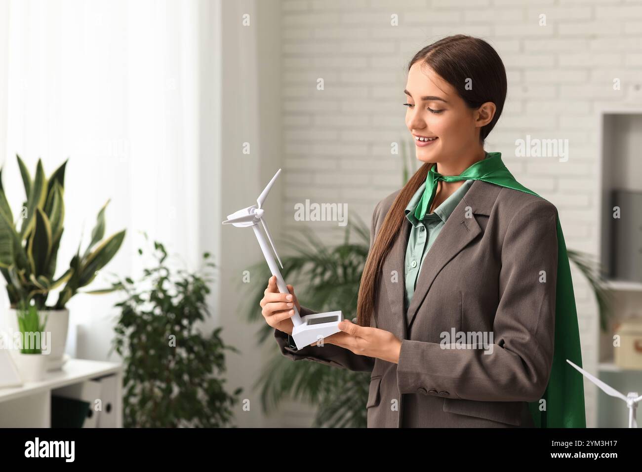 Female engineer with superhero cape and wind turbine model in office ...