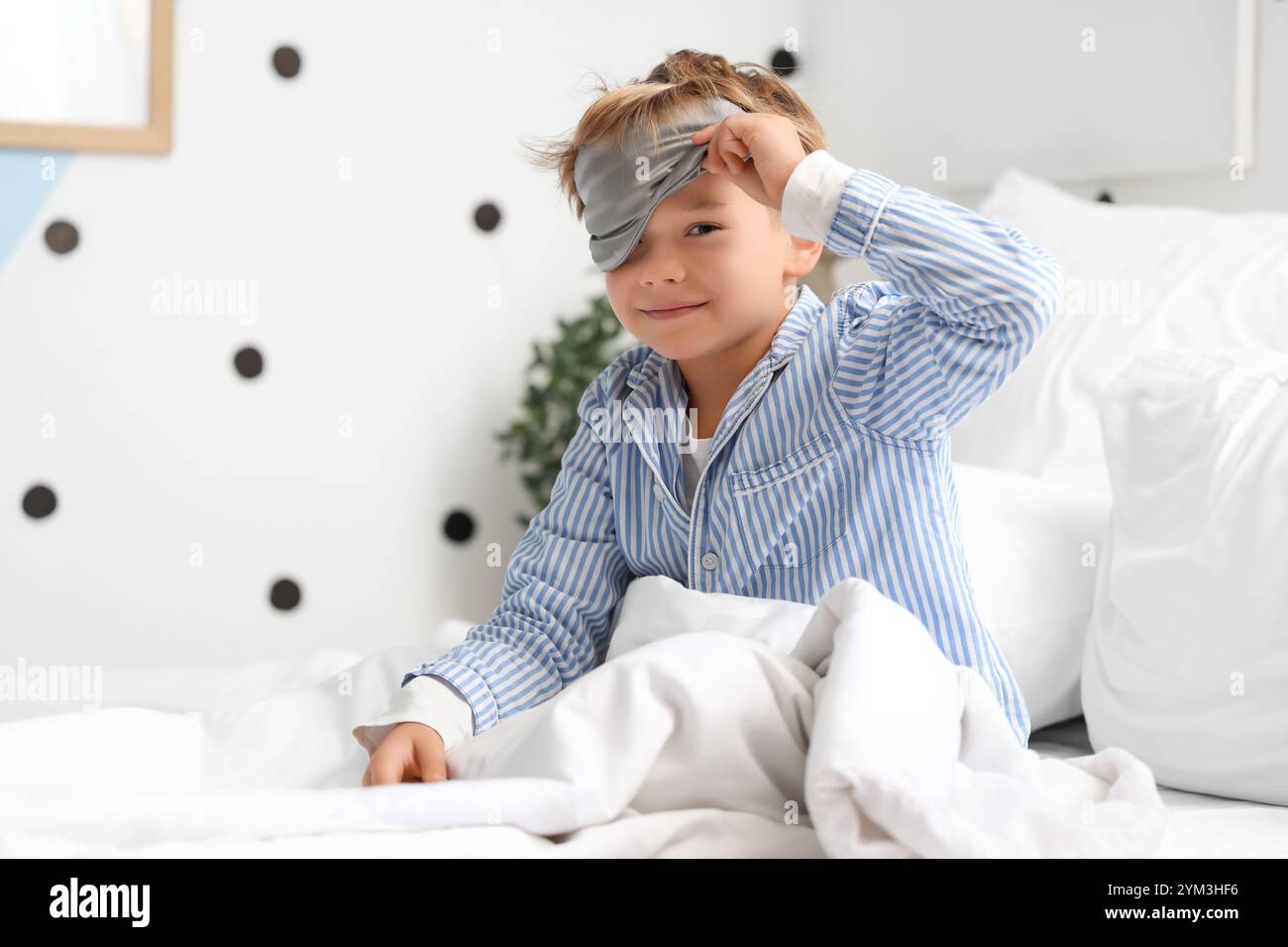 Morning of cute little boy in pajamas with sleeping mask sitting on bed ...