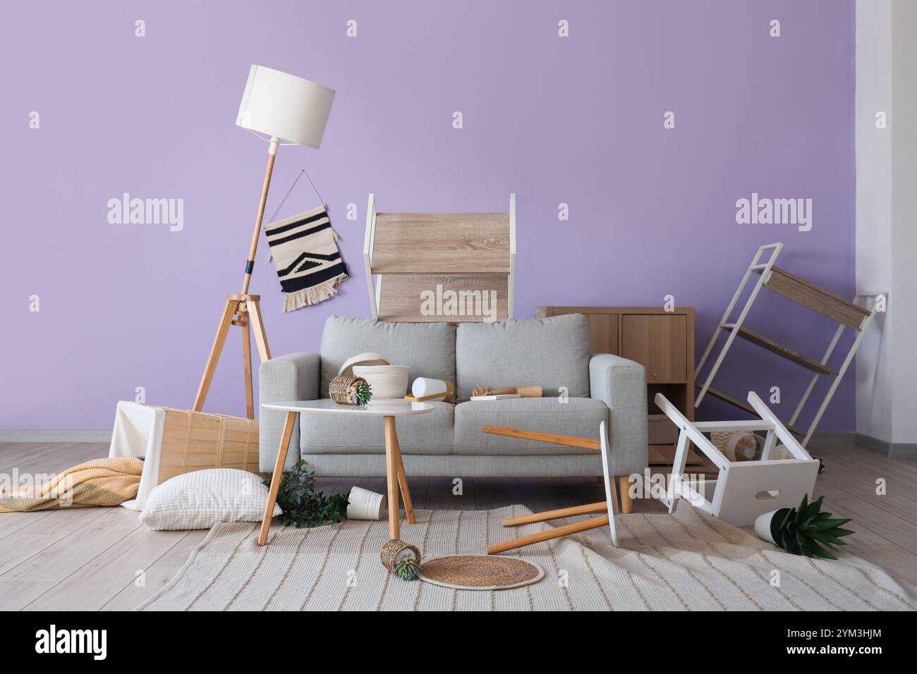 Interior of messy living room with grey sofa and overturned furniture ...