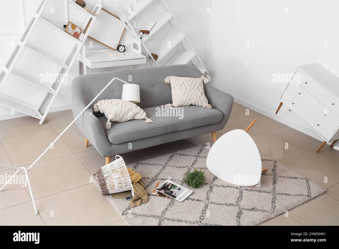 Interior of messy living room with grey sofa, overturned coffee table ...