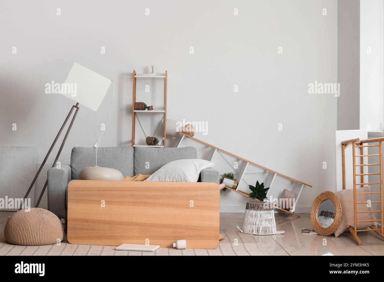 Interior of messy living room with grey sofa and overturned furniture ...