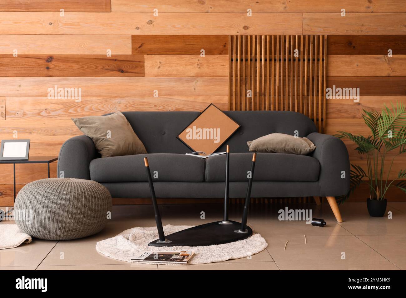 Interior of messy living room with grey sofa, pouf and overturned ...