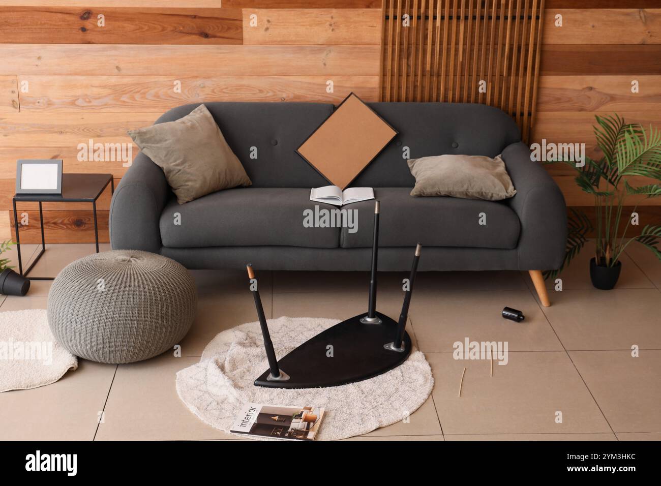 Interior of messy living room with grey sofa, pouf and overturned ...