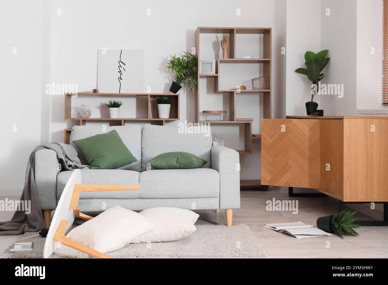 Interior of messy room with grey sofa and overturned furniture after ...