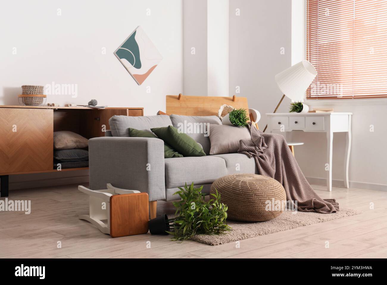 Interior of messy room with grey sofa and overturned furniture after ...