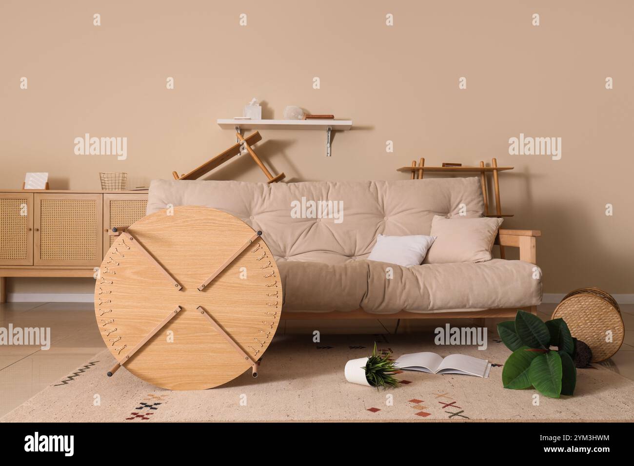 Interior of messy room with beige sofa and overturned furniture after ...