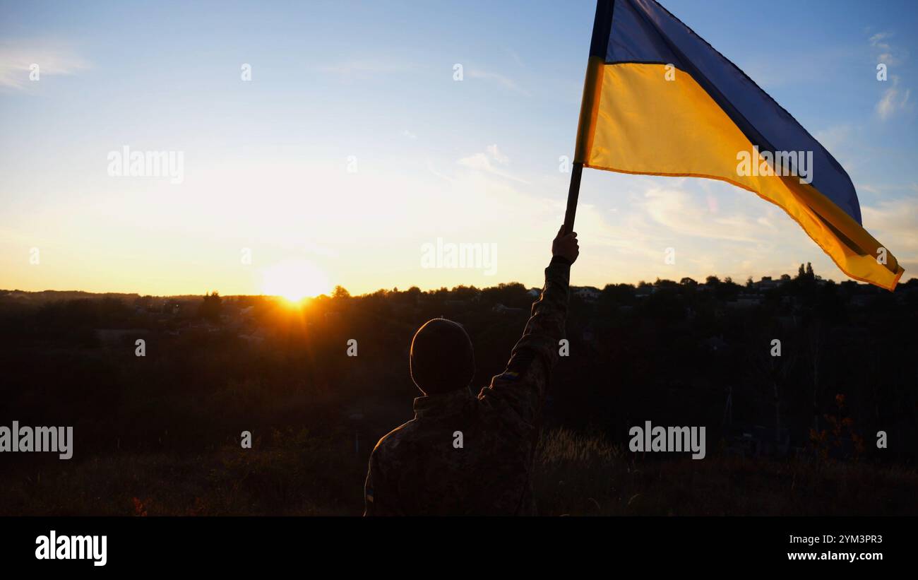 Male soldier stands with raised flag of Ukraine against background of ...