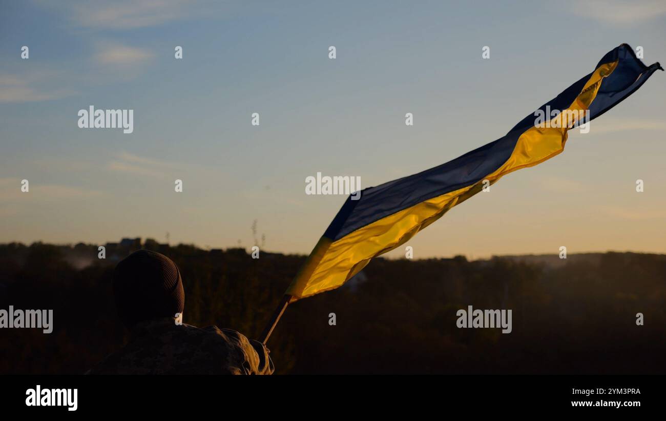 Young man in military uniform waving flag of Ukraine against beautiful ...