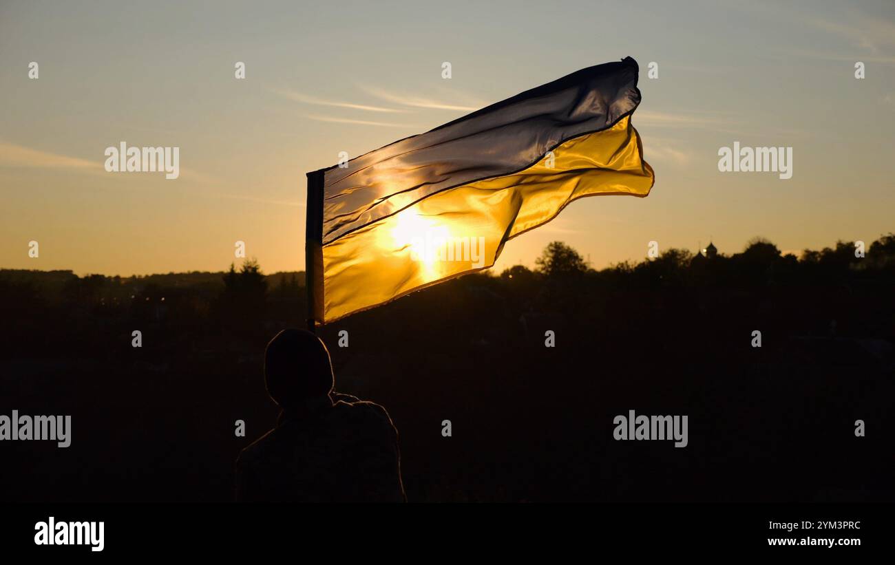 Young man in military uniform waving flag of Ukraine against beautiful ...