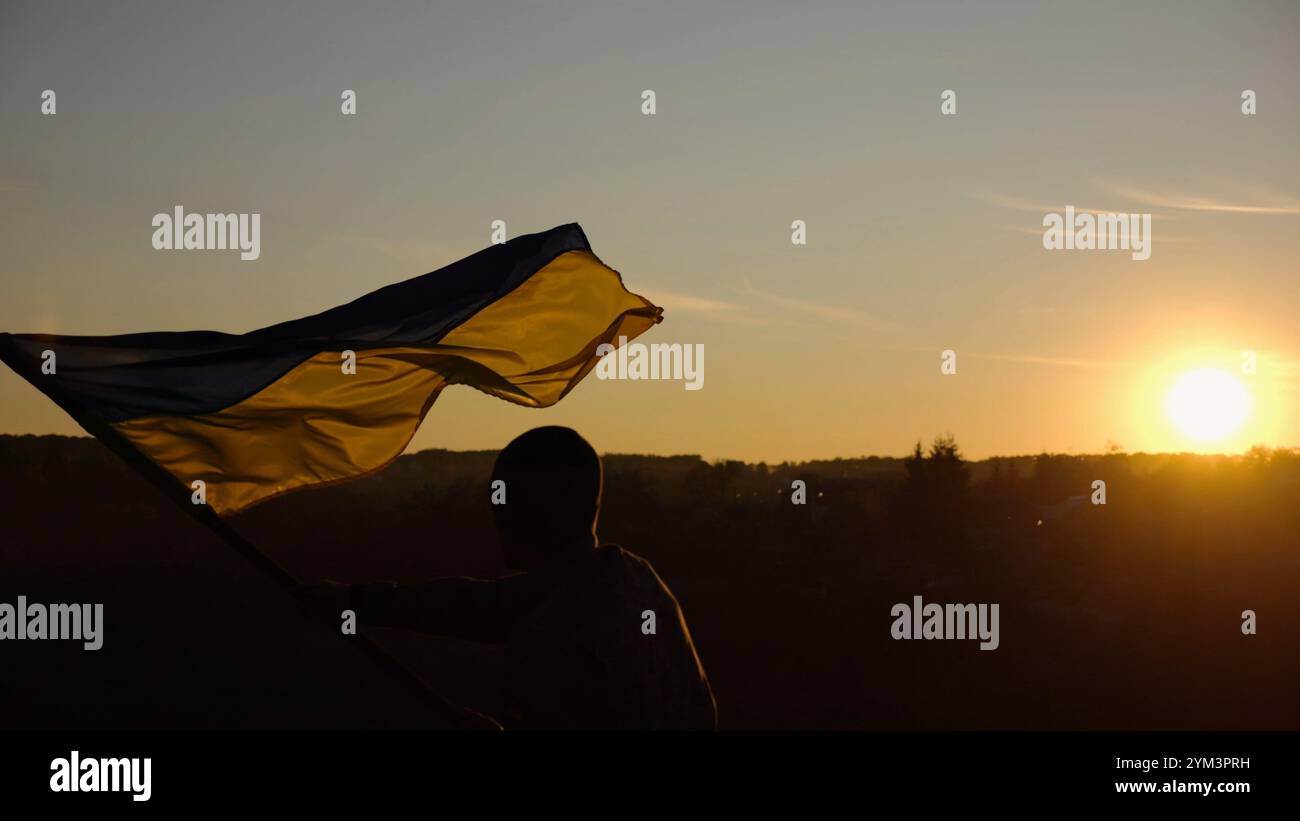 Young man in military uniform waving flag of Ukraine against beautiful ...