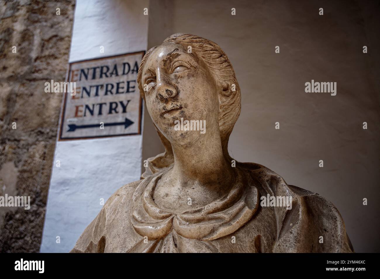 A weathered stone statue in front of signage of entry in a small ...